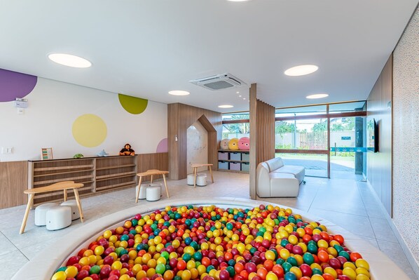 Espaço infantil com piscina de bolinhas, assentos e vista para o exterior.