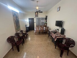 Uma sala de jantar com mesa posta para seis pessoas, rodeada por cadeiras, um ventilador de teto e uma televisão na parede.