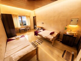 Quarto de hotel com duas camas de solteiro, uma escrivaninha, uma cadeira, uma mesinha, pia e espelho.