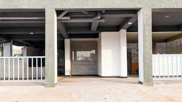 Entrada de um edifício com um portão de metal fechado, pilares de concreto e chão pavimentado.