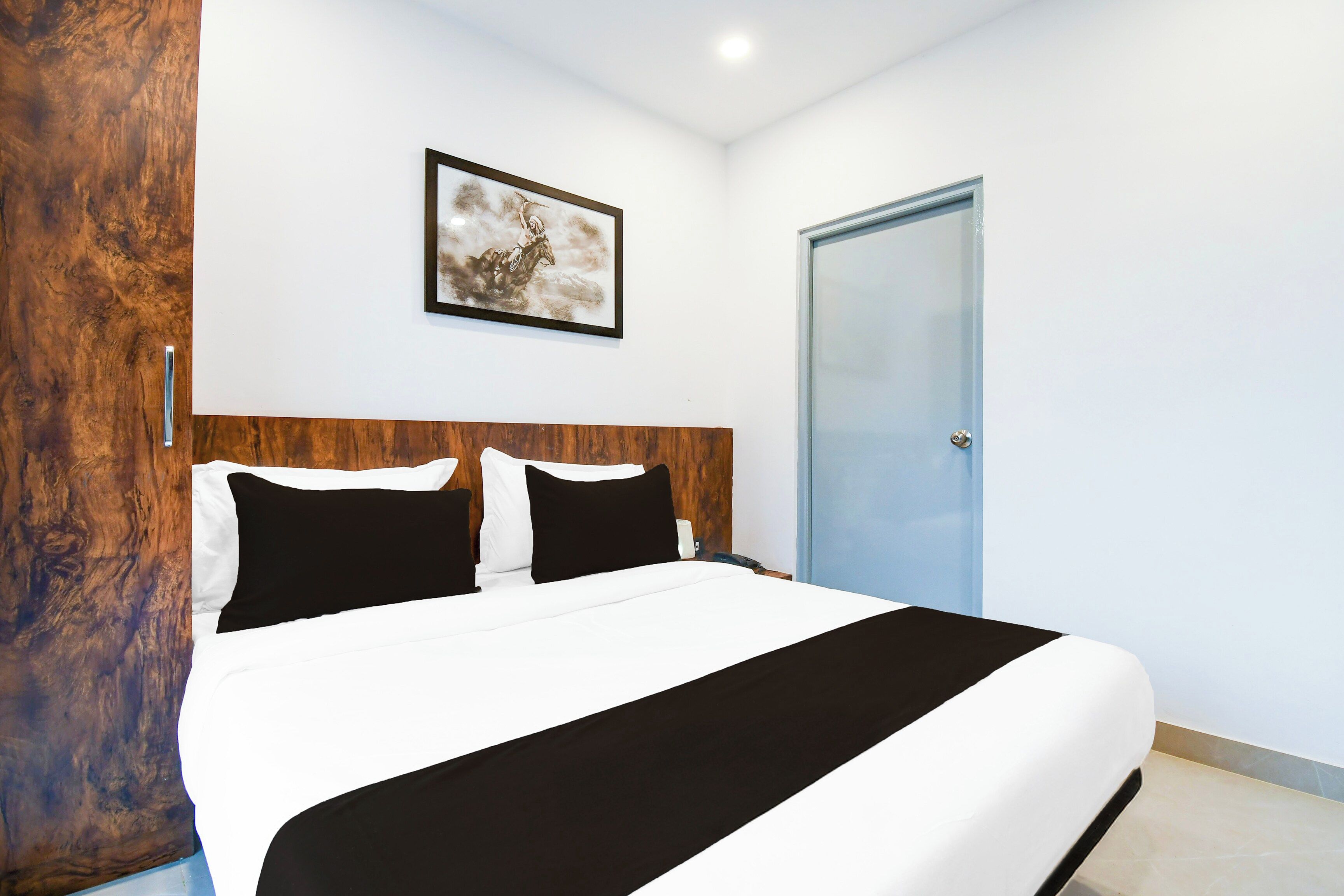 Quarto de hotel com uma cama grande, cabeceira de madeira, um quadro na parede e uma porta.