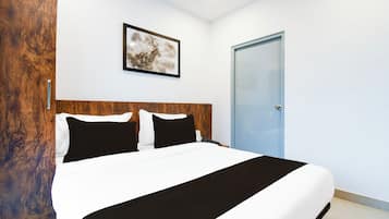 Quarto de hotel com uma cama grande, cabeceira de madeira, um quadro na parede e uma porta.