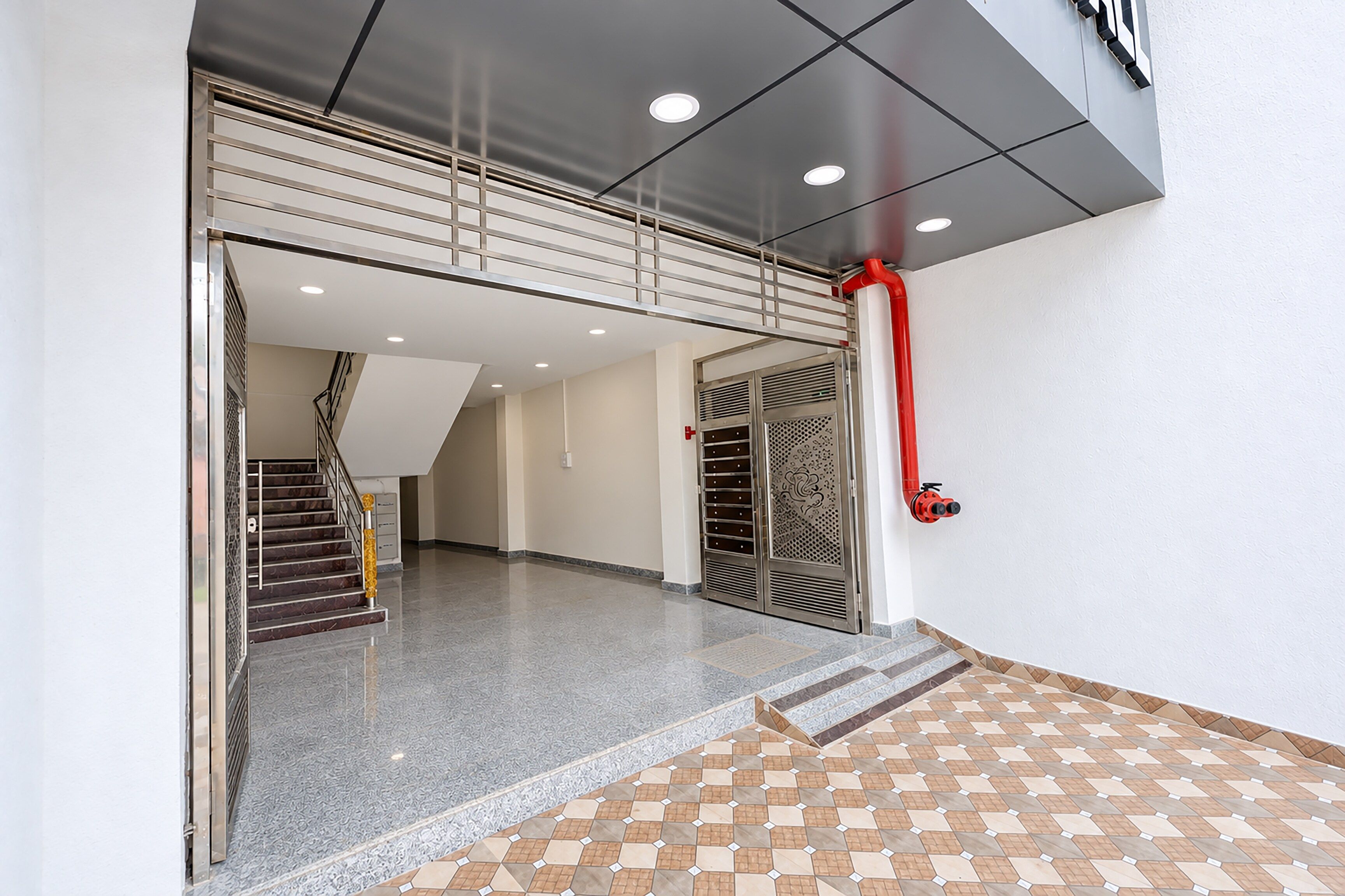 Interior moderno com escada que leva a um andar superior, mangueira de incêndio na parede e piso estampado.
