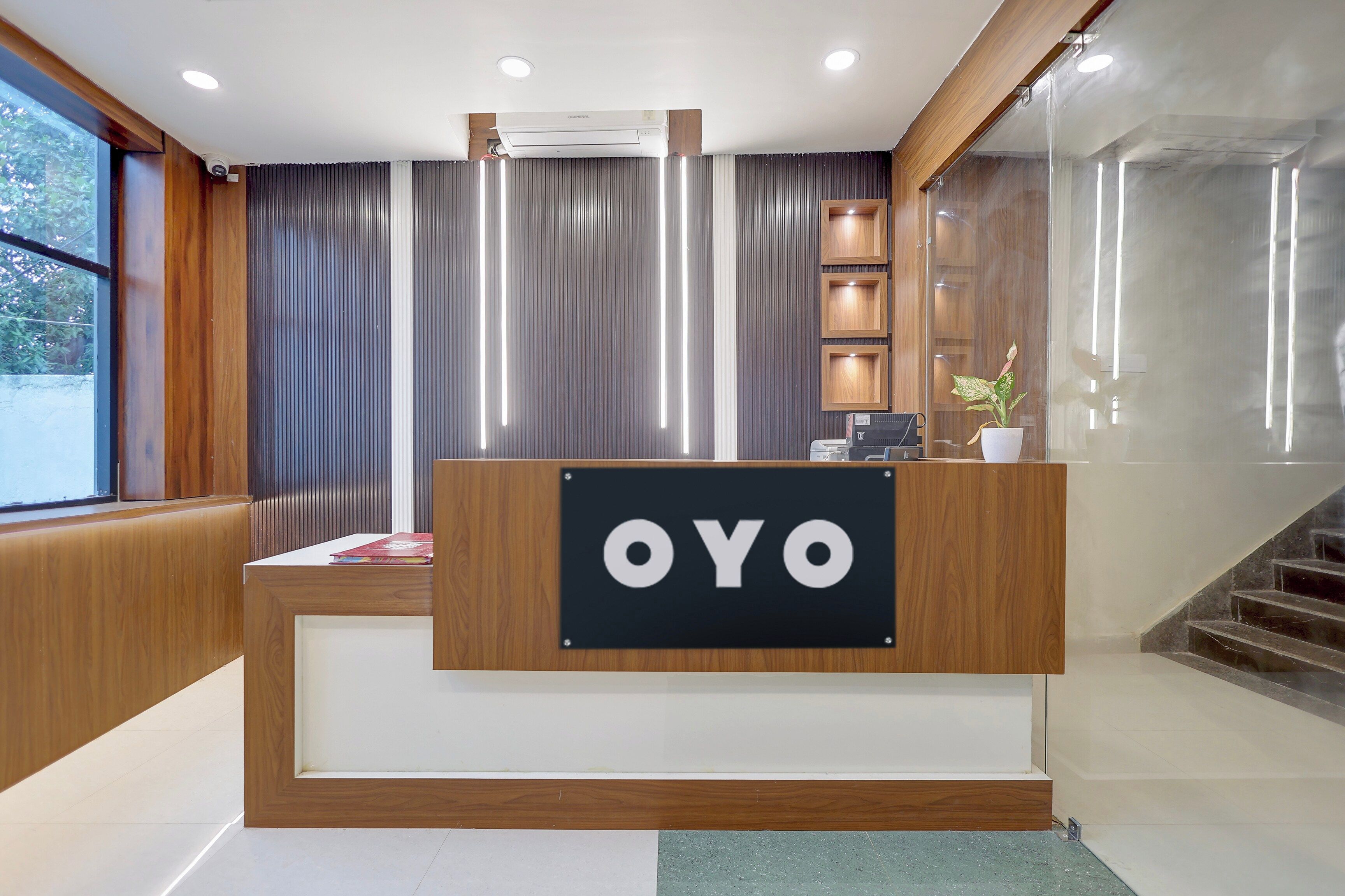 Bancada de recepção com placa indicando 'OYO' em um moderno hall de hotel com lambris de madeira e uma escadaria.