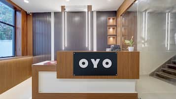 Bancada de recepção com placa indicando 'OYO' em um moderno hall de hotel com lambris de madeira e uma escadaria.