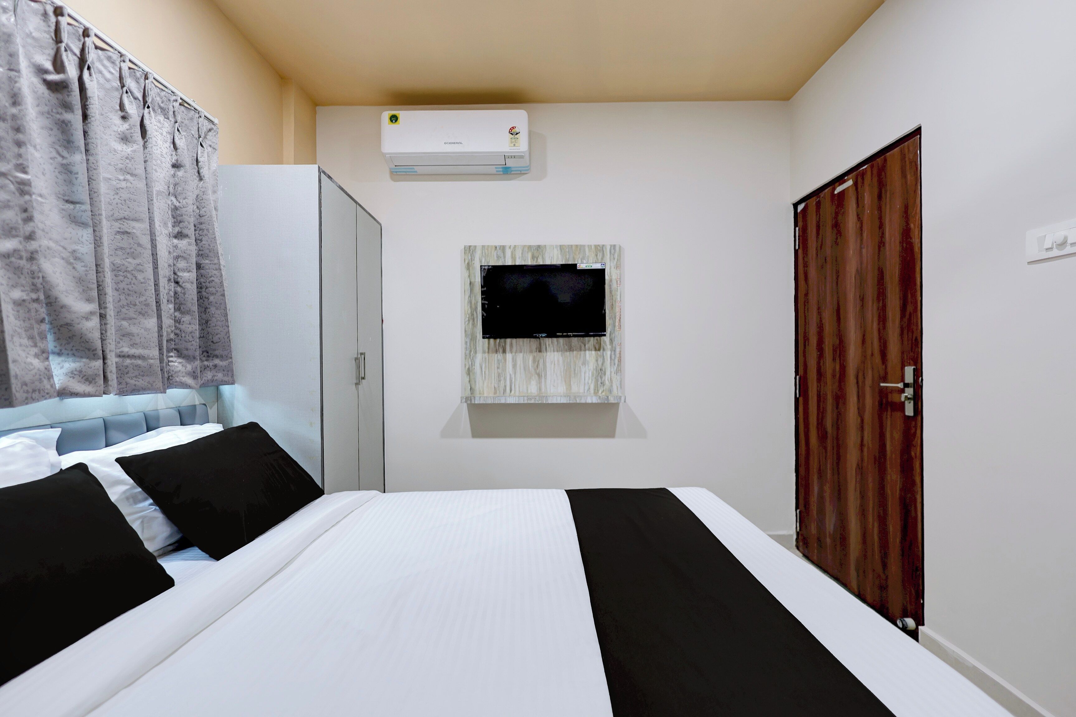 Quarto de hotel com cama, guarda-roupa, televisão na parede e aparelho de ar condicionado.