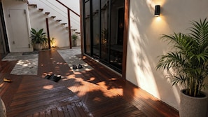 Um deck de madeira com escada, vasos de plantas e luminária fixada na parede.
