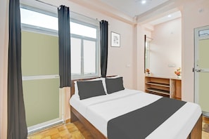 Quarto com cama, janela com cortinas, mesa de cabeceira com um vaso de flores e guarda-roupa.