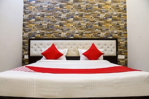 Uma cama com cabeceira estofada, duas almofadas vermelhas e um edredom branco.