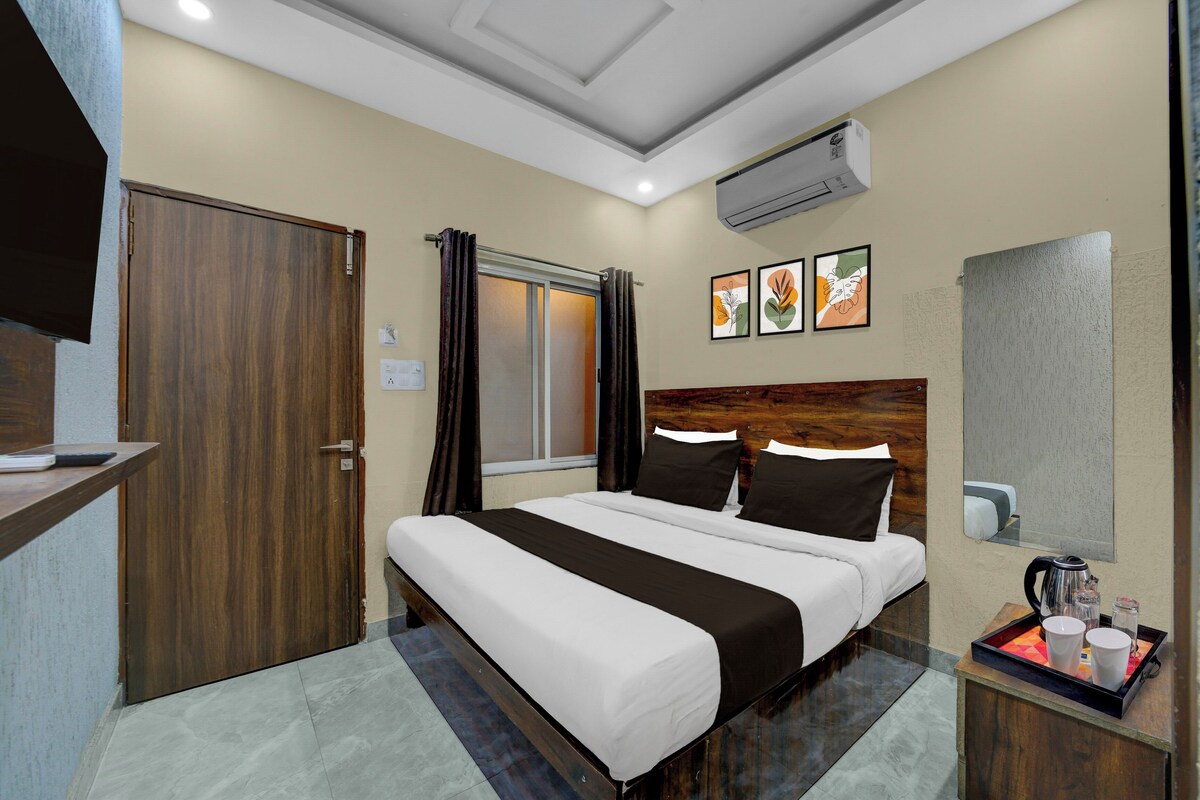 Quarto de hotel com cama, mesa de cabeceira com bandeja de copos, janela com cortinas e ar condicionado fixado na parede.