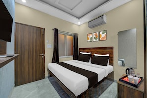 Quarto de hotel com cama, mesa de cabeceira com bandeja de copos, janela com cortinas e ar condicionado fixado na parede.