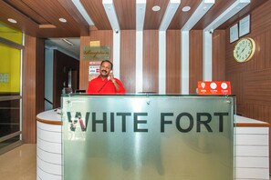 Bancada de recepção com a inscrição 'WHITE FORT', um relógio e um aviso de 'PROIBIDO FUMAR' acima.