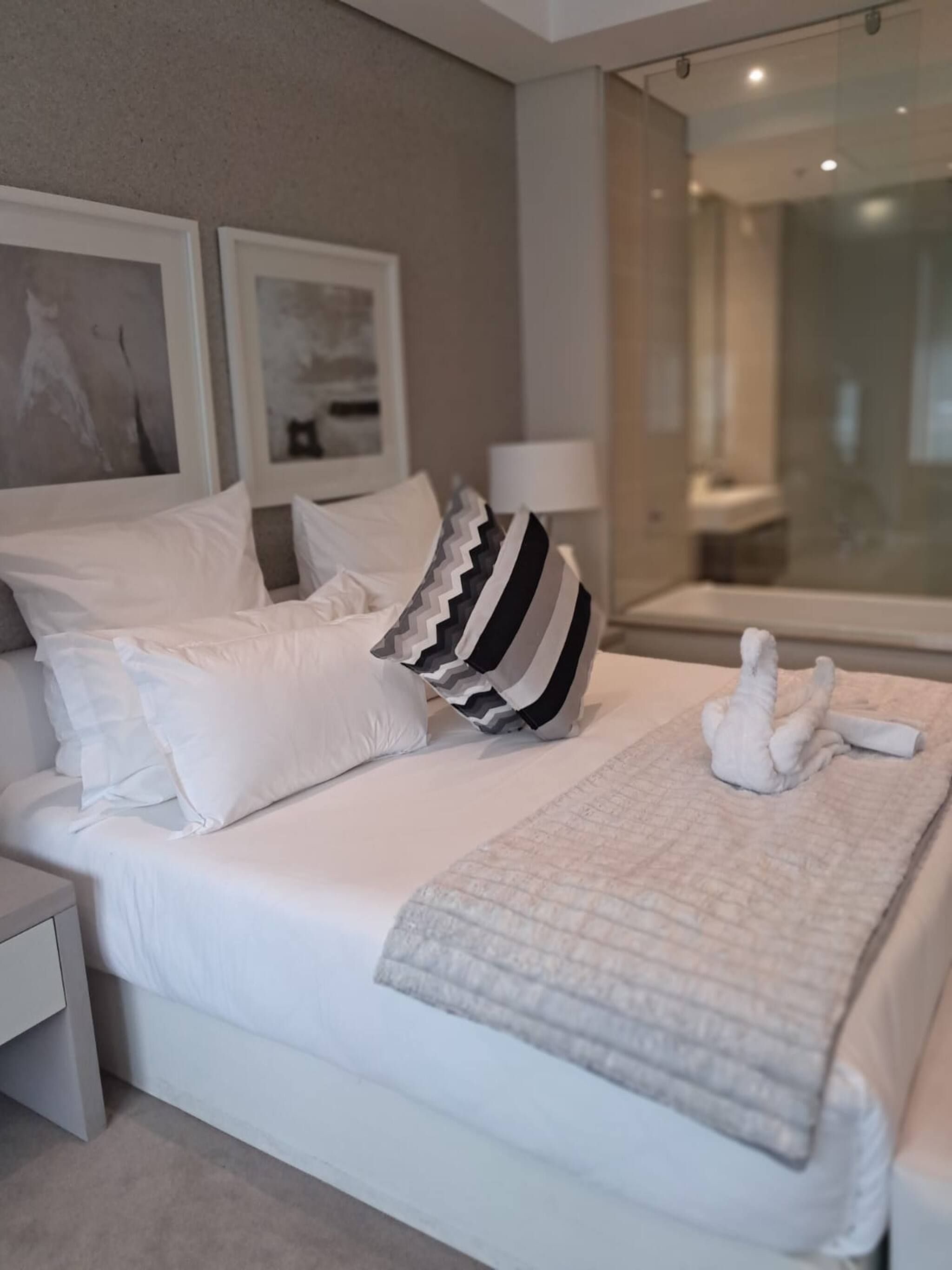 Cama bem arrumada com roupa de cama branca e travesseiro listrado, mesa de cabeceira e parede com duas fotos emolduradas.