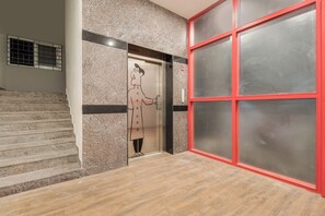Um saguão de hotel com uma escada, uma porta com um personagem de desenho animado e uma janela com moldura vermelha.
