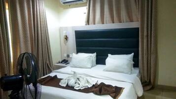 Quarto de hotel com cama, cortinas, ar condicionado e ventilador.