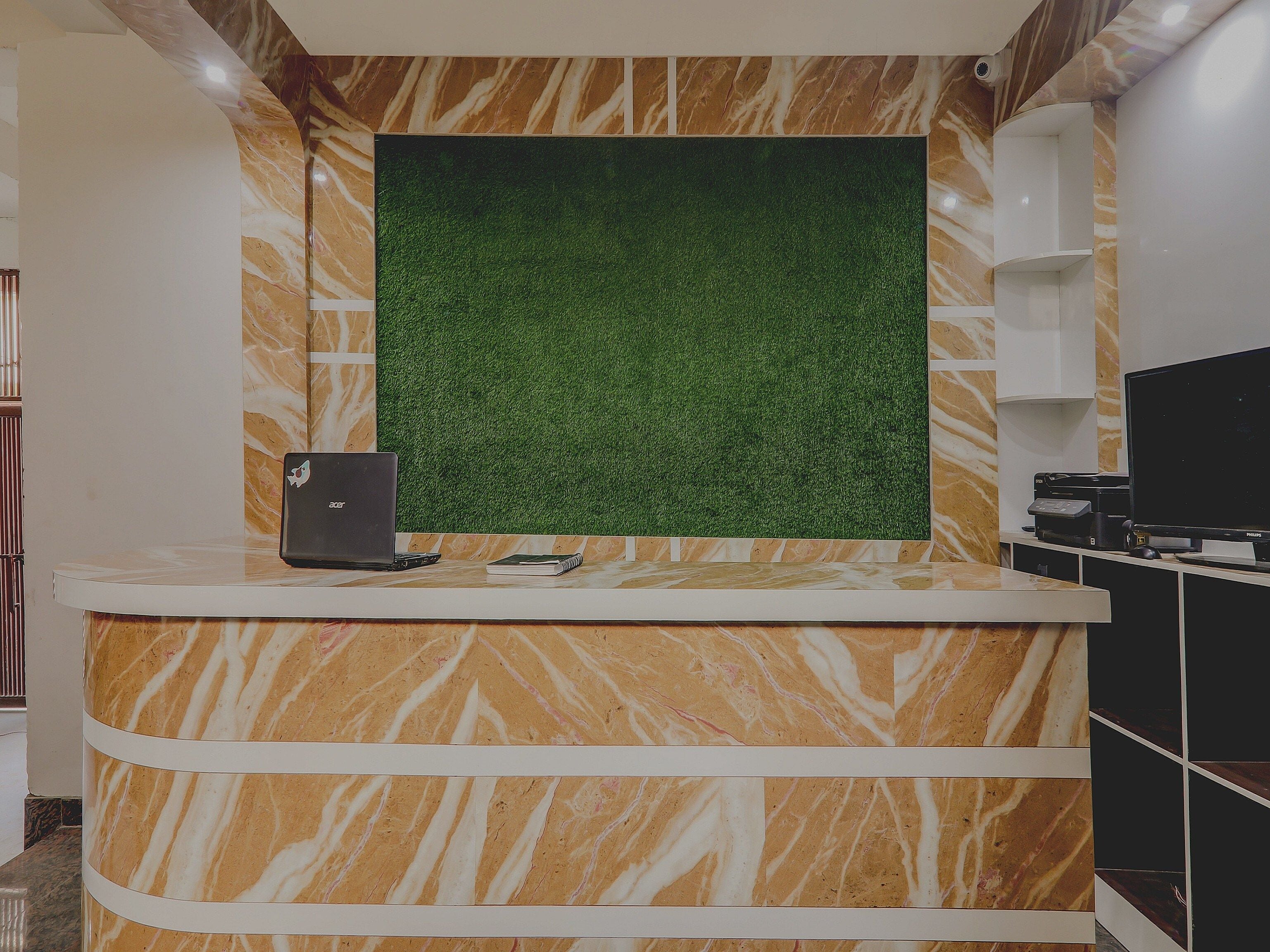 Balcão de recepção com parede de grama sintética verde, um laptop e uma televisão de tela plana.