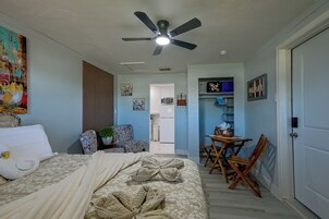 Quarto com cama, ventilador de teto, área de jantar com mesa e cadeiras, e cozinha ao fundo.
