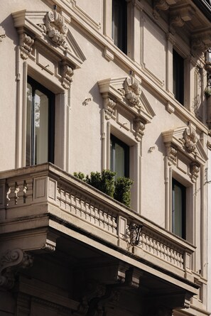 Fachada de edifício com detalhes arquitetônicos ornamentados, incluindo molduras decorativas e uma varanda com grades de ferro forjado.