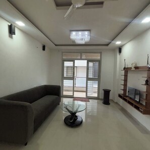 Uma sala de estar com um sofá, uma mesa de centro de vidro e um ventilador de teto.