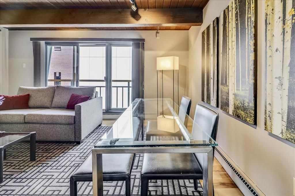 Uma sala de estar moderna com mesa de vidro, poltronas de couro, um sofá e uma janela grande com vista.