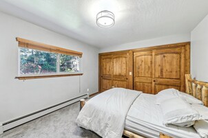Quarto com cama, janela com persianas, luminária no teto e armários de madeira.