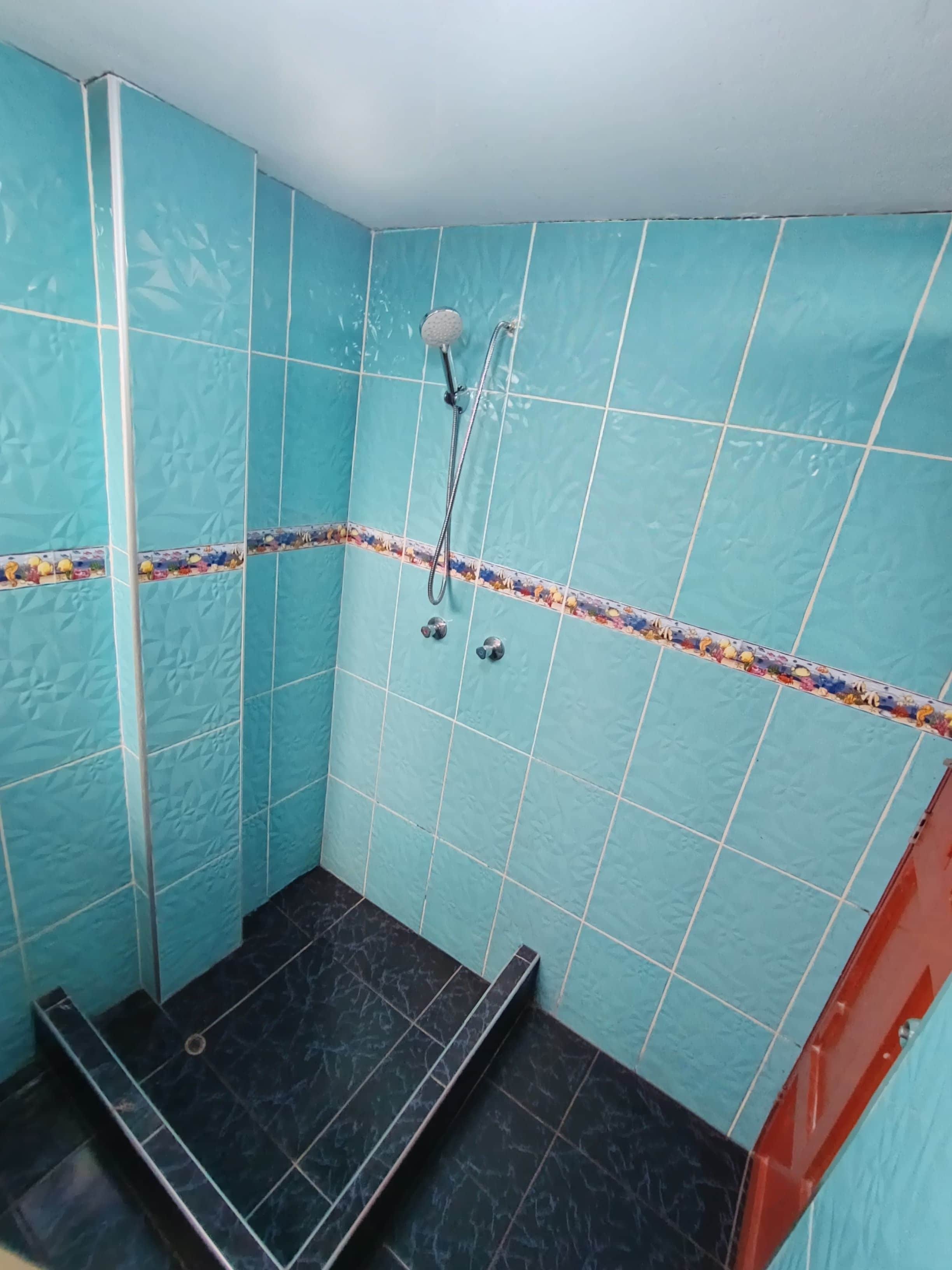 Área de chuveiro com azulejos azuis e piso de mármore preto.