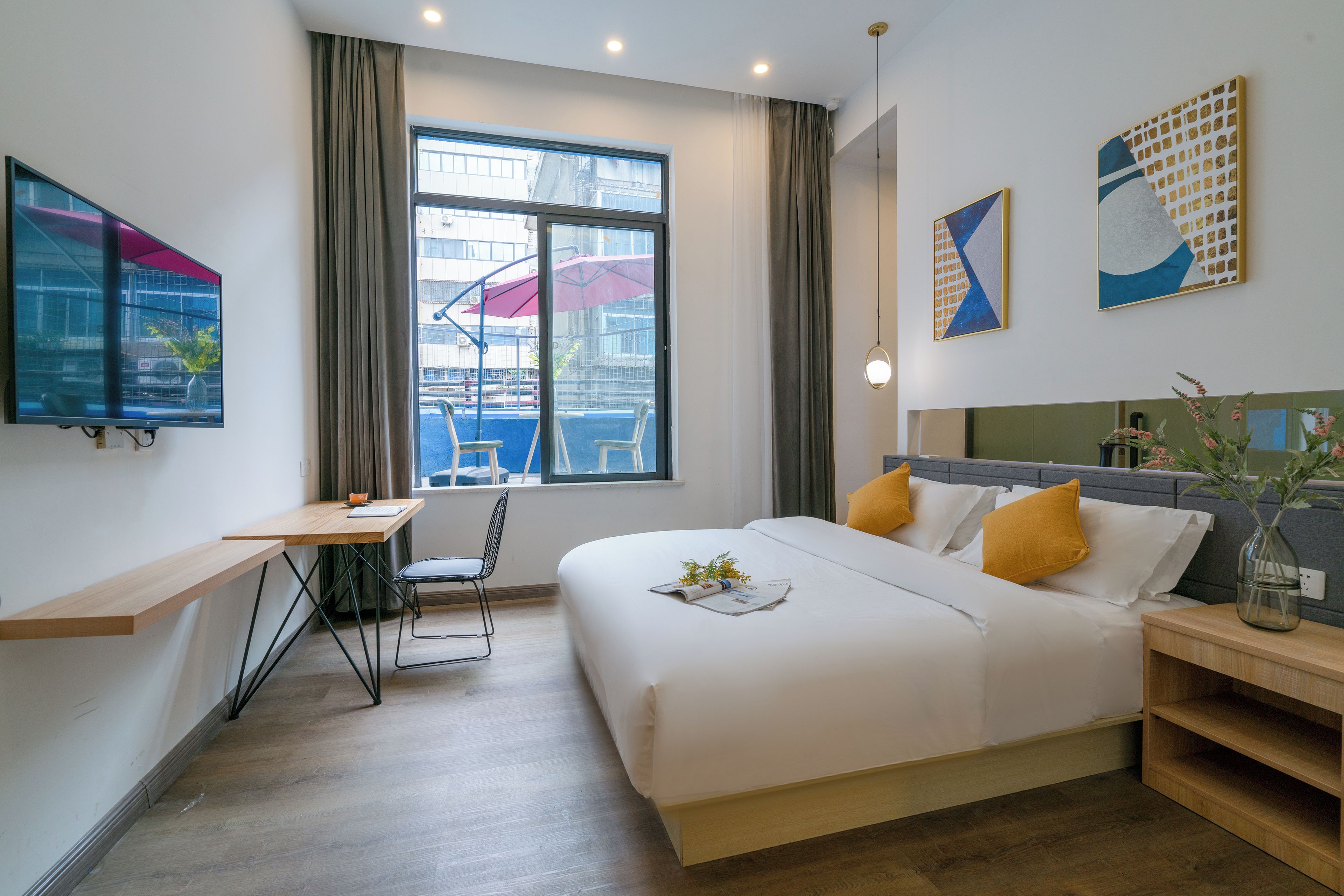 Quarto de hotel com cama, escrivaninha, cadeira e janela com vista para edifícios.
