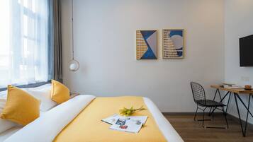 Quarto de hotel com cama, escrivaninha e duas pinturas na parede.