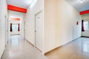 Um corredor com uma porta branca, detalhes vermelhos no teto e um extintor de incêndio fixado na parede.