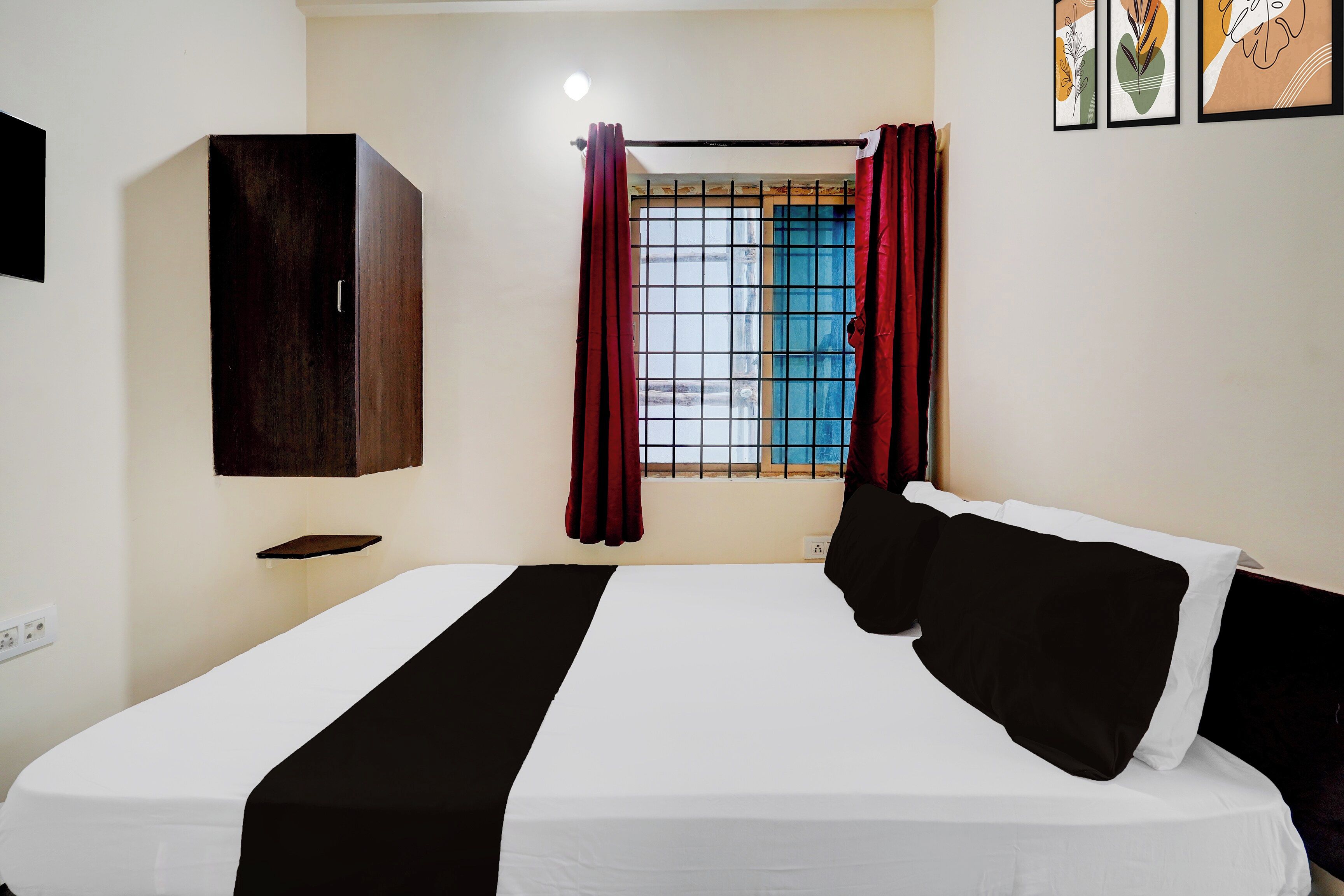 Quarto de hotel com cama, guarda-roupa, janela com cortinas e parede decorada com quadros.