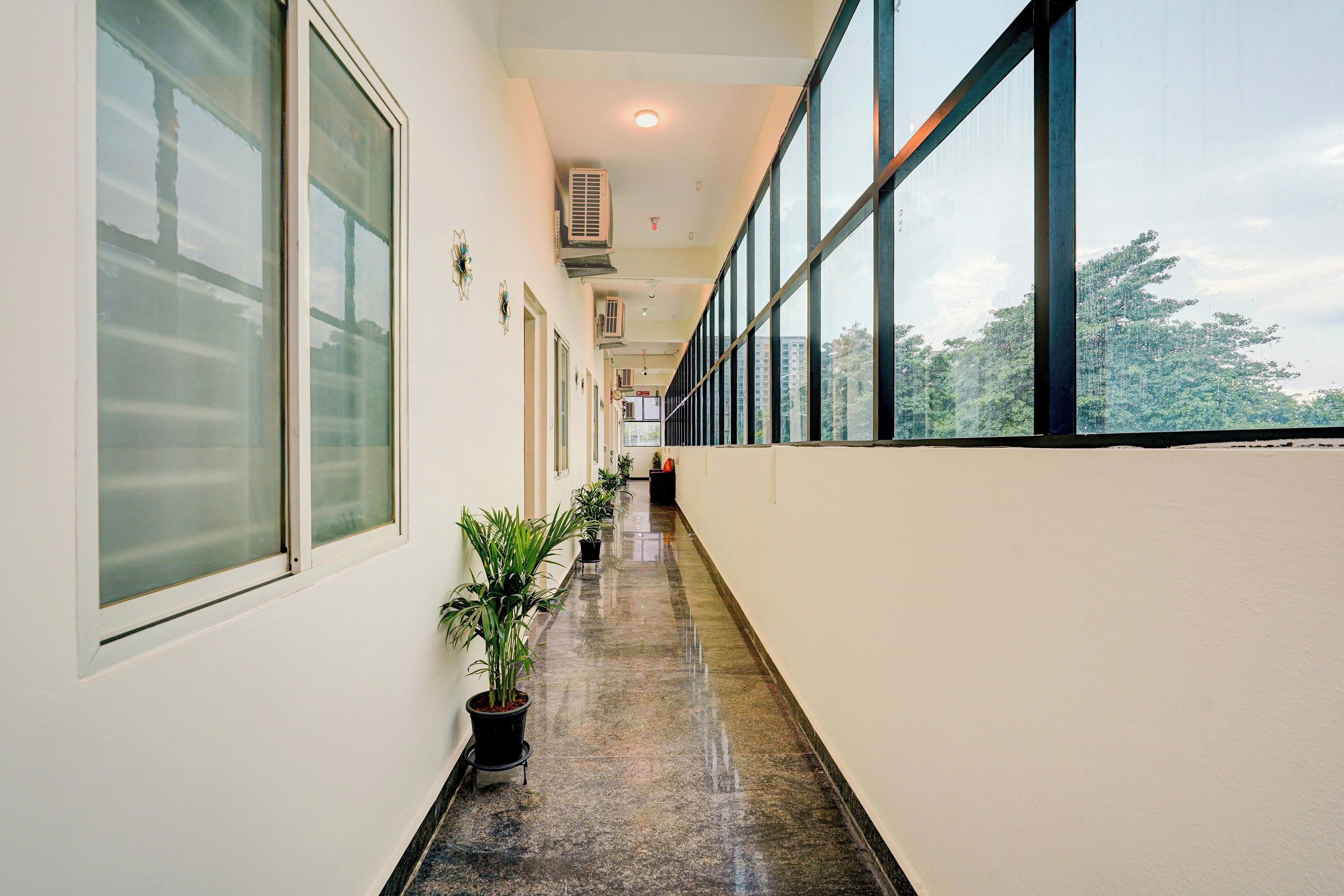 Um corredor com amplas janelas, plantas em vasos e piso lustroso.