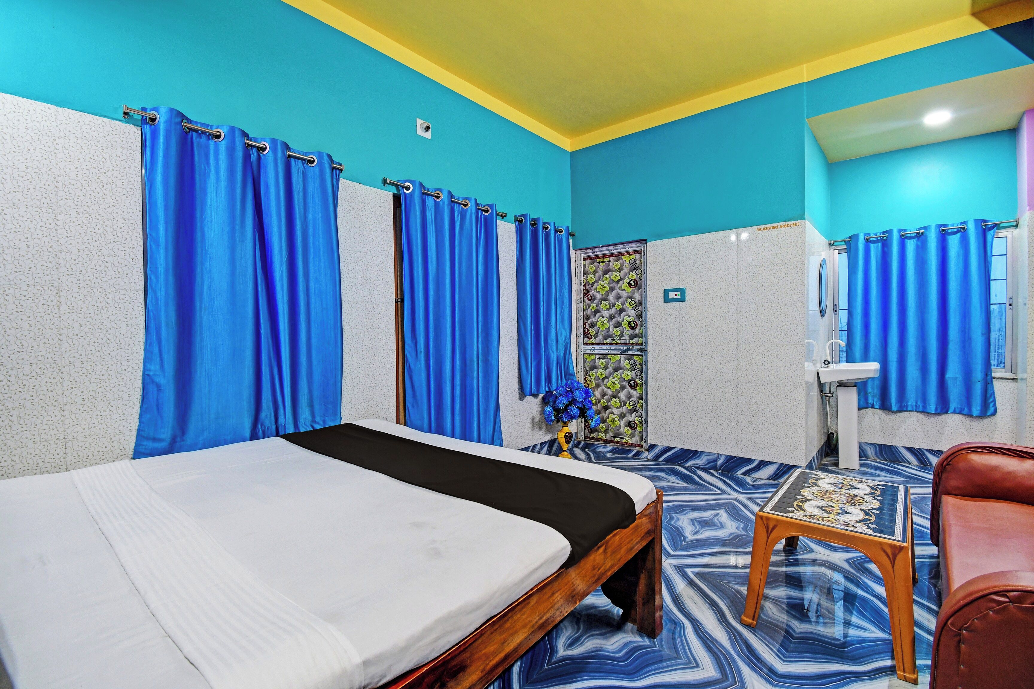 Quarto com cama, cadeira, pia e janela com cortinas.