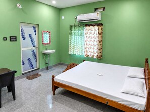 Quarto com cama, mesa de cabeceira, ar condicionado fixado na parede, janela com cortinas e porta com isolamento.