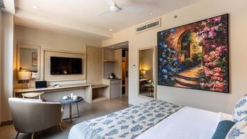 Quarto de hotel com cama, escrivaninha, cadeira, televisão e um quadro.