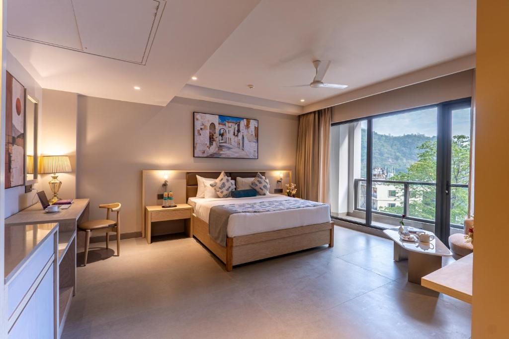 Quarto de hotel moderno com cama grande, escrivaninha, cadeira, mesa de cabeceira e vista para o exterior.