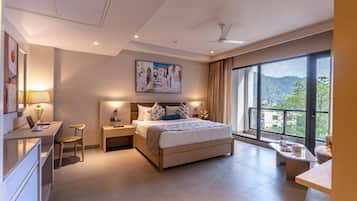 Quarto de hotel moderno com cama grande, escrivaninha, cadeira, mesa de cabeceira e vista para o exterior.