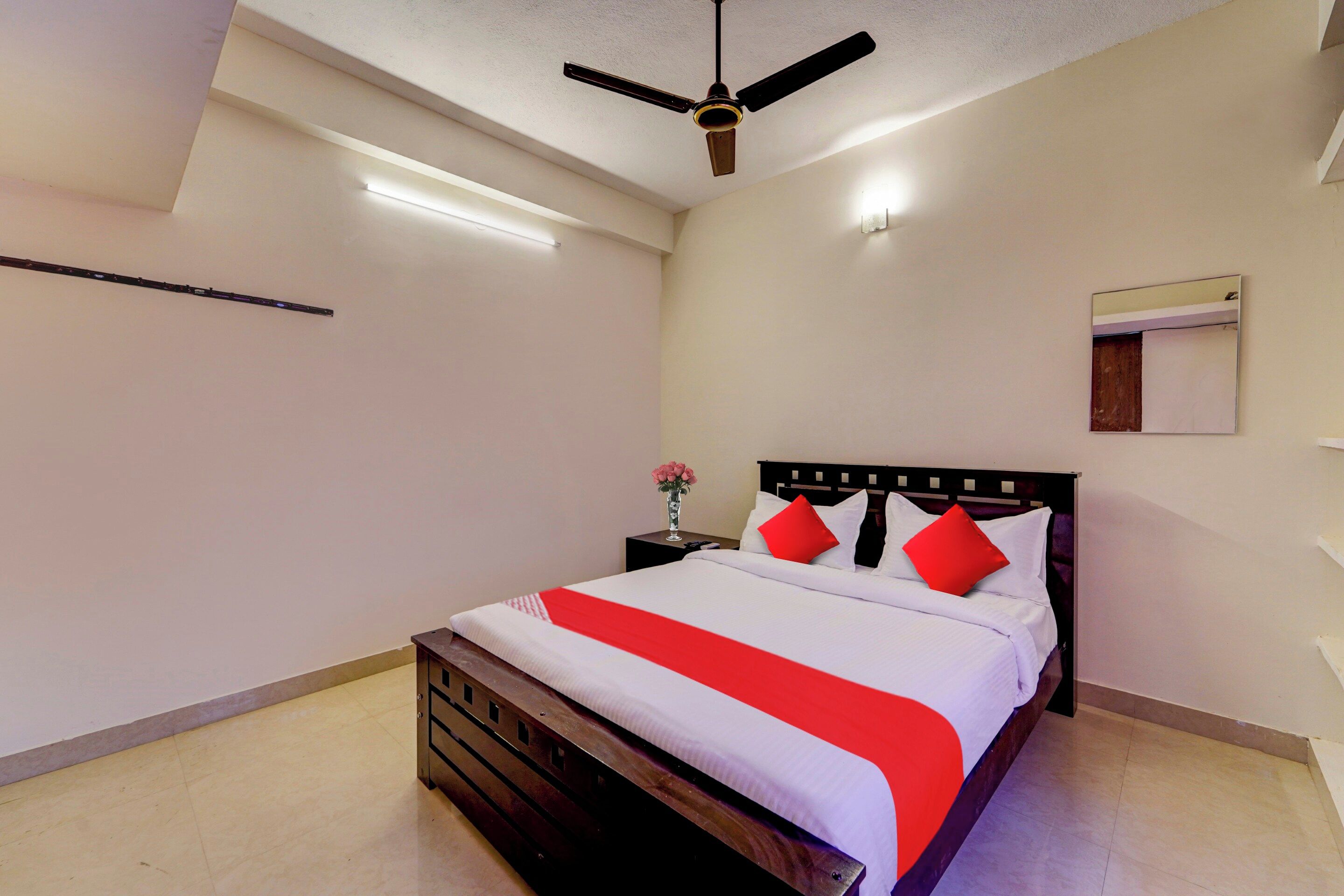 Quarto de hotel com cama, mesa de cabeceira, vaso com flores, ventilador de teto e luminária fixada na parede.
