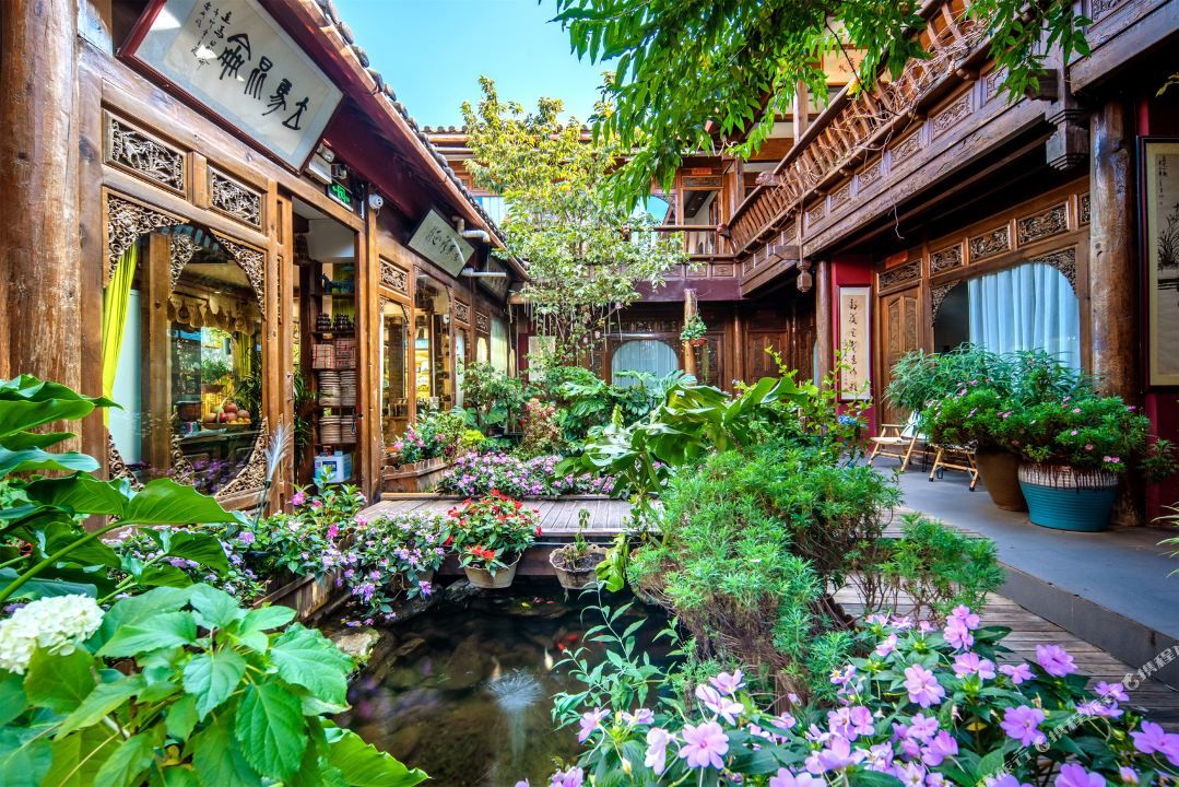 Um pátio tradicional com um pequeno lago, edifícios de madeira e diversas plantas.