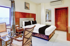 Quarto de hotel com cama, poltrona, mesinha, espelho e ar-condicionado.