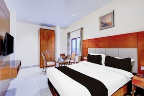 Quarto de hotel com uma cama grande, televisão, escrivaninha e uma cadeira.