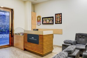 Balcão de recepção com uma placa indicando 'OYO TOWNHOUSE', um calendário fixado na parede e um quadro religioso emoldurado.