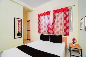 Quarto com cama, mesa de cabeceira, espelho e janela com cortinas.