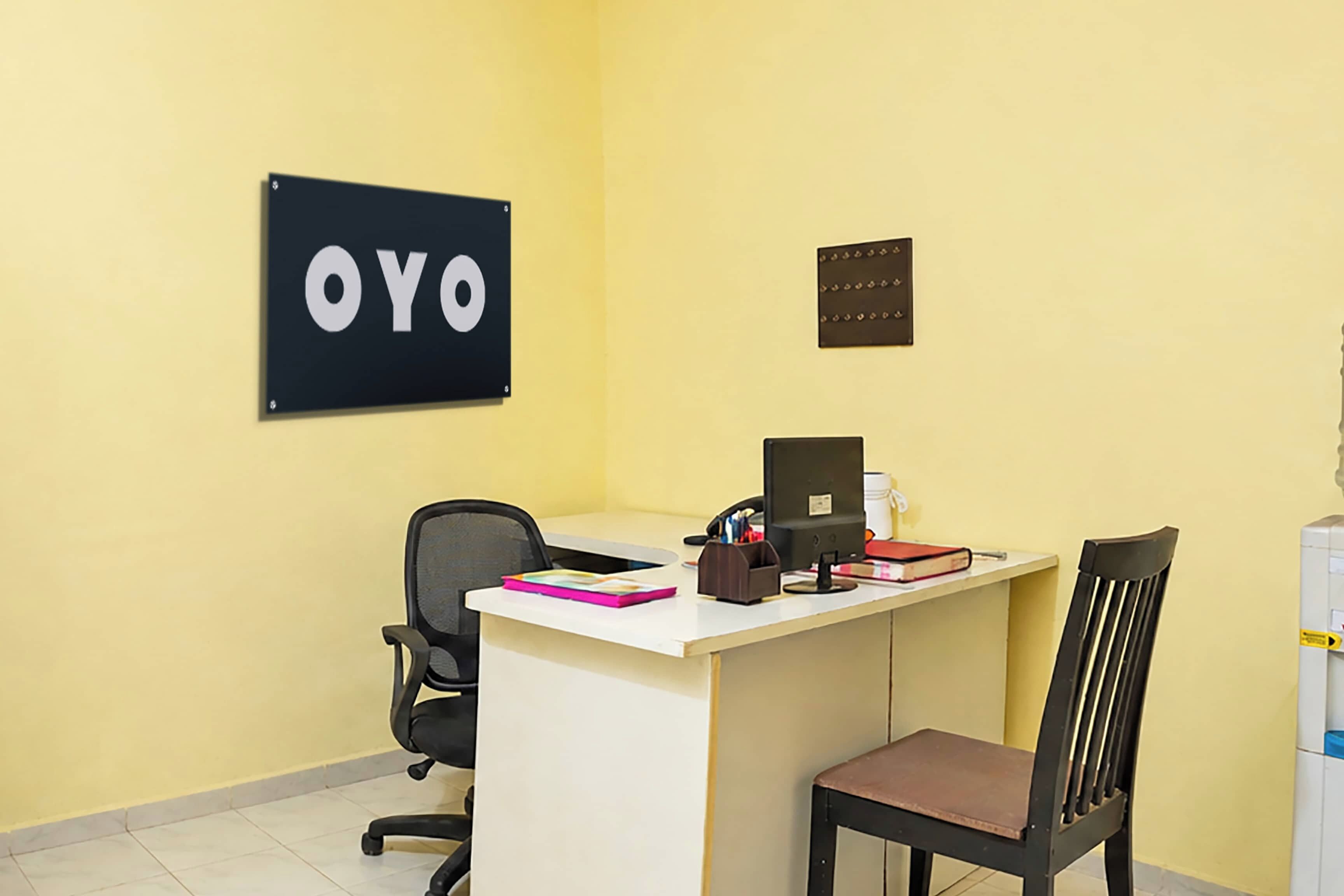 Um quarto com escrivaninha, cadeira, computador e uma placa com a inscrição 'OYO'.