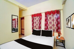 Quarto de hotel com cama, mesa de cabeceira, espelho e janela com cortinas vermelhas.