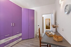 Quarto com um guarda-roupa roxo, uma mesa de jantar com um tabuleiro de chávenas e um relógio na parede.