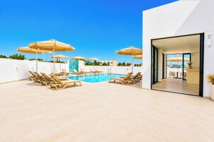 Área de piscina no terraço com espreguiçadeiras e guarda-sóis, céu azul e vista da cidade.
