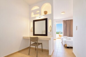 Quarto de hotel com escrivaninha, cadeira, espelho grande e cama com vista para a cidade.