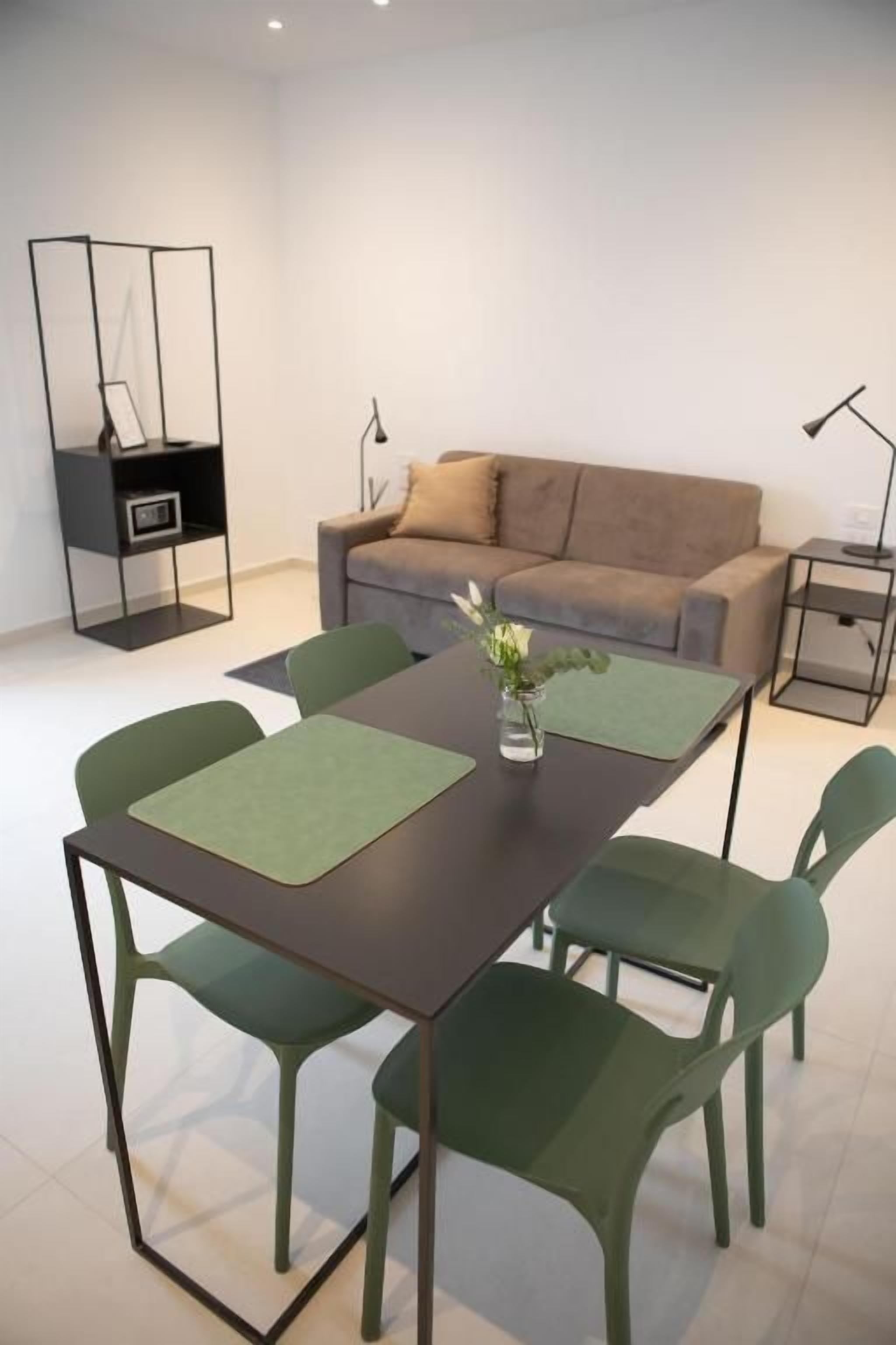 Uma sala de estar moderna com um sofá, uma mesa de jantar com cadeiras, um abajur e uma estante alta preta.