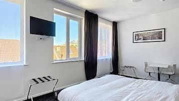 Quarto de hotel com cama, televisão de tela plana, escrivaninha com cadeira e janela com cortinas.