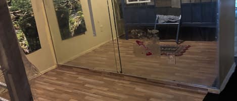 Quarto com porta de vidro que dá para o exterior, piso de madeira, toldo listrado e uma pequena área de estar ao ar livre.